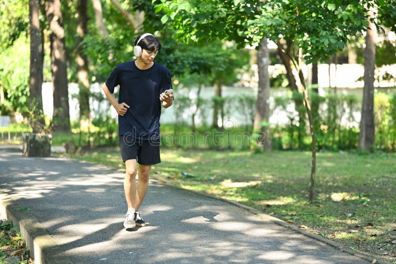 Active Man Holding a Smartphone Jogging on Shaded Pathway in City Park ...