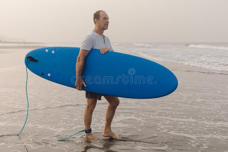 Surfboarder Carrying a Surfboard in the Wavy Ocean Near the Wooden Pier ...
