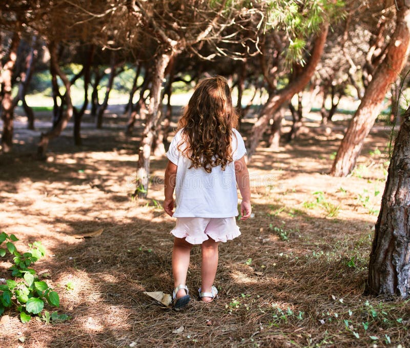 Adorable Blonde Child on Back View Standing Around Trees on the Park ...