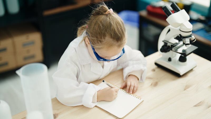 Adorable Blonde Girl Student Using Microscope Writing on Notebook at ...