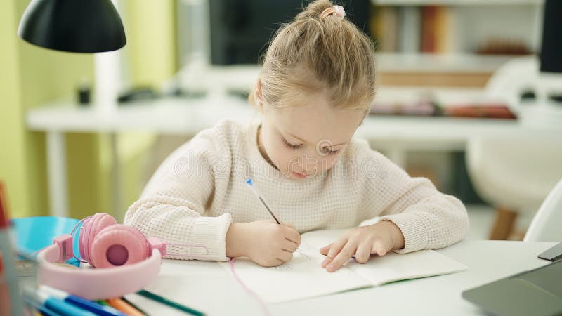 Adorable Blonde Girl Student Writing on Notebook Sitting on Table at ...