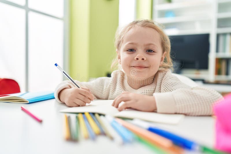 Adorable Blonde Girl Student Writing on Notebook Sitting on Table at ...