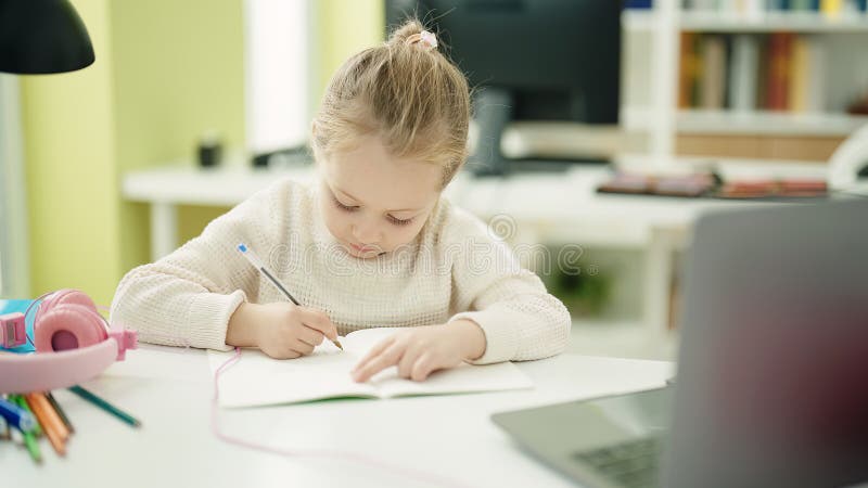 Adorable Blonde Girl Student Writing on Notebook Sitting on Table at ...