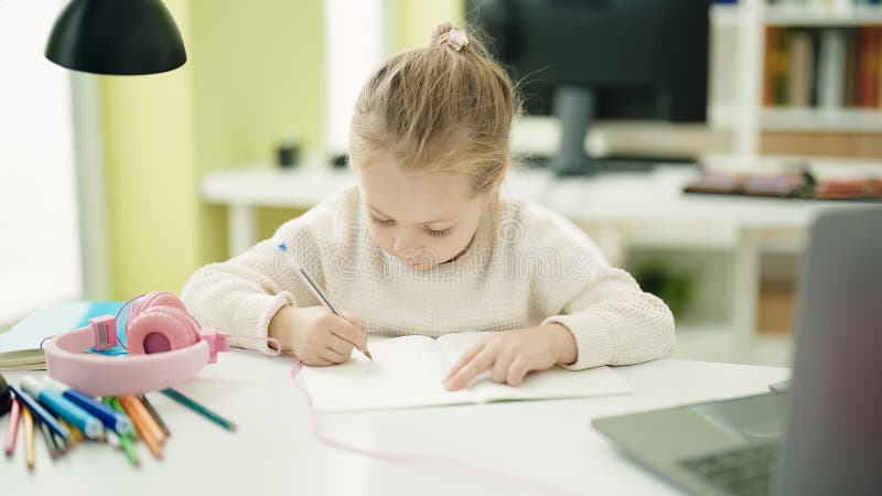 Adorable Blonde Girl Student Writing on Notebook Sitting on Table at ...