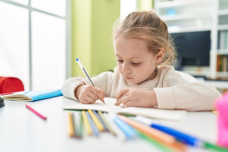 Adorable Blonde Girl Student Writing on Notebook Sitting on Table at ...