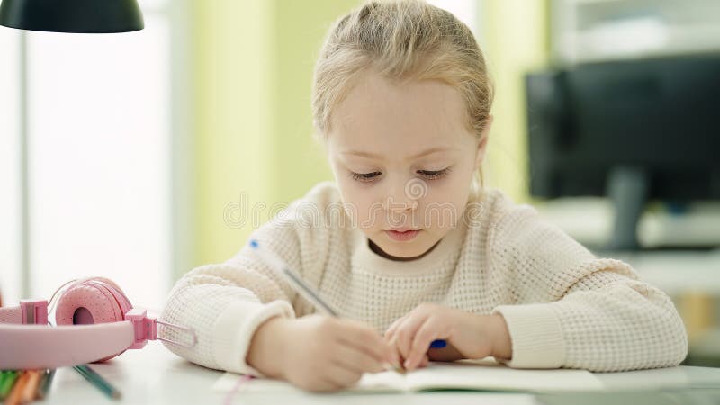 Adorable Blonde Girl Student Writing on Notebook Sitting on Table at ...