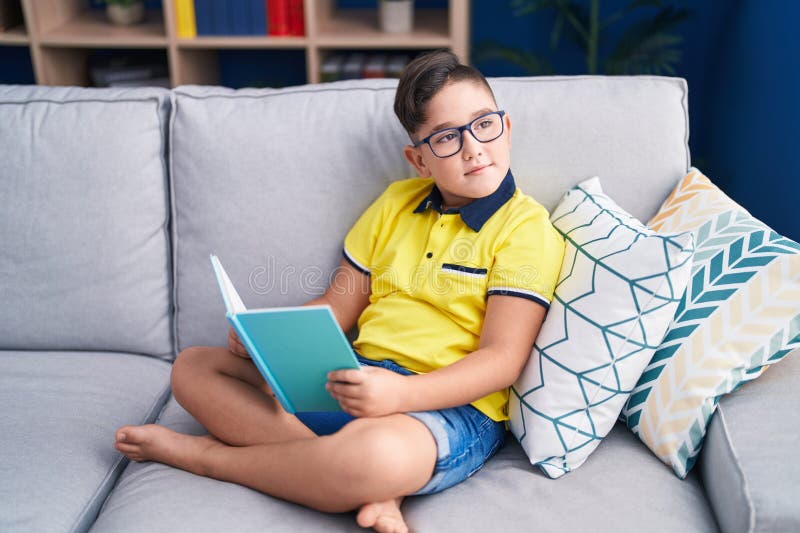 Adorable Hispanic Boy Reading Book Sitting on Sofa at Home Stock Photo ...