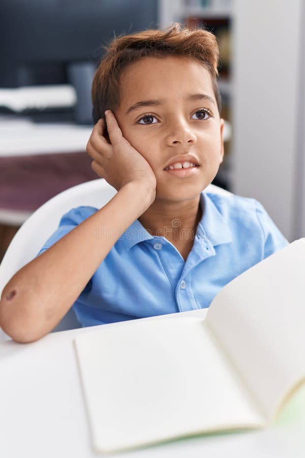 Adorable Hispanic Boy Student Reading Book Thinking at Classroom Stock ...