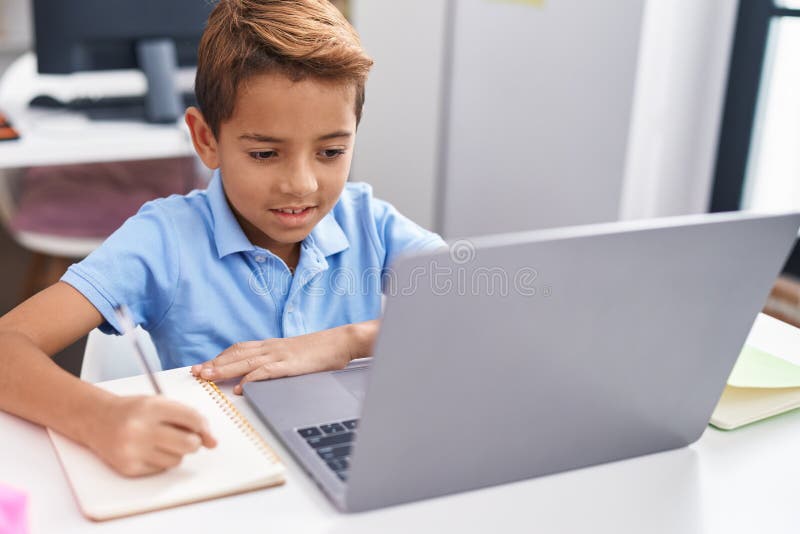 Adorable Hispanic Boy Student Using Computer Writing on Notebook at ...