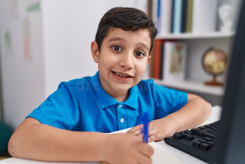 Adorable Hispanic Boy Student Using Computer Writing on Notebook at ...