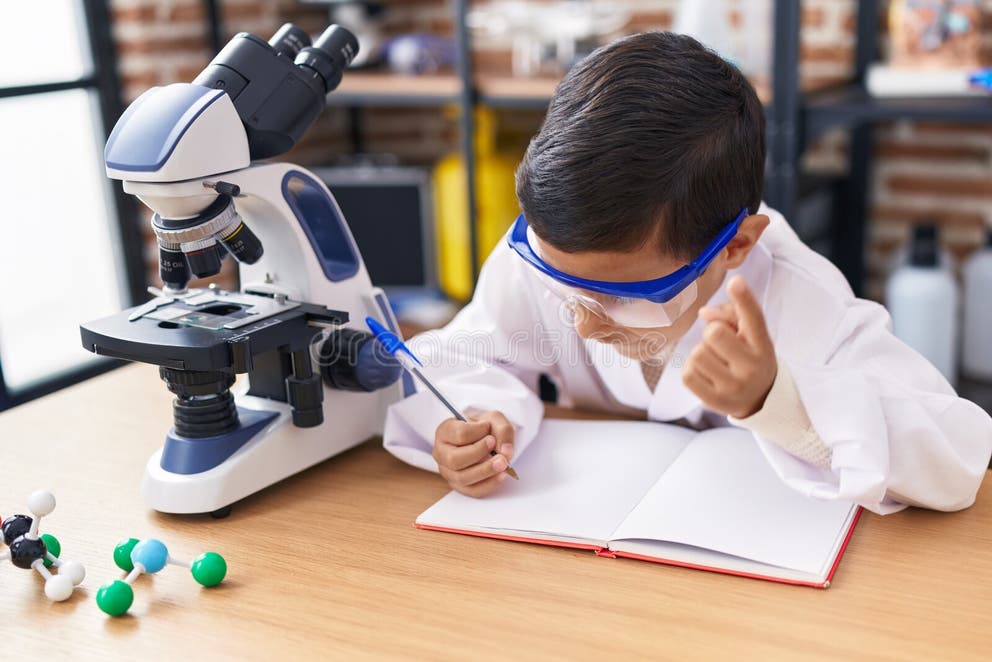 Adorable Hispanic Boy Student Using Microscope Writing on Notebook at ...