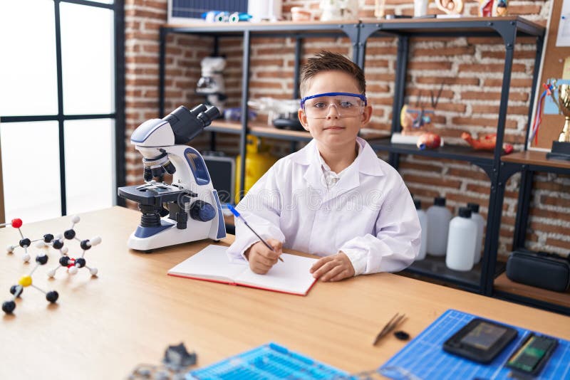 Adorable Hispanic Boy Student Using Microscope Writing on Notebook at ...