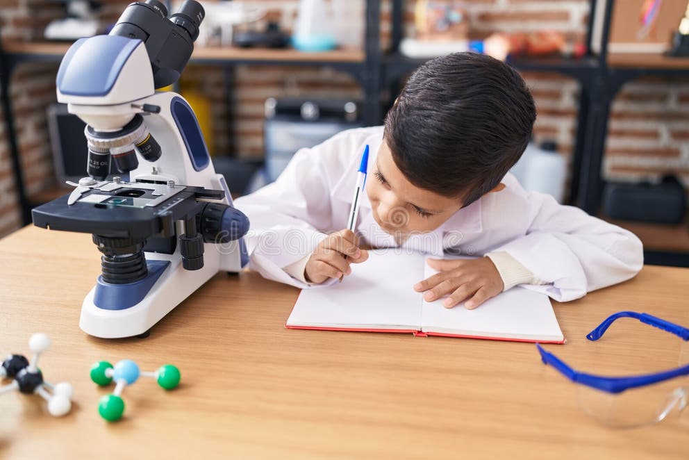 Adorable Hispanic Boy Student Using Microscope Writing on Notebook at ...