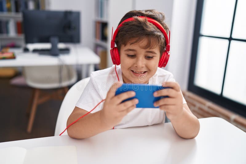 Adorable Hispanic Boy Student Using Smartphone and Headphones at ...