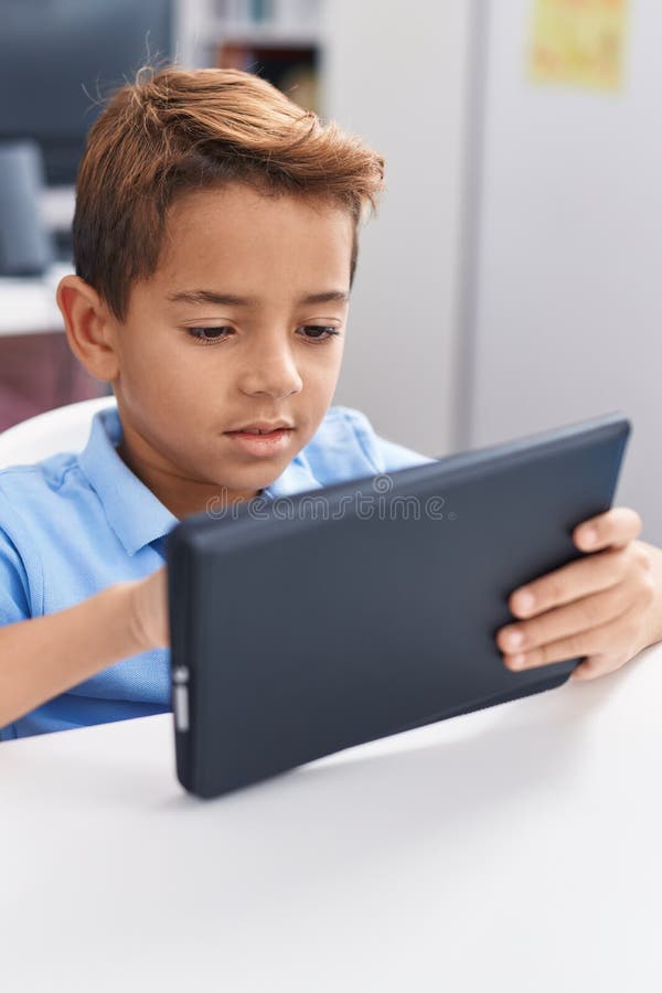 Adorable Hispanic Boy Student Using Touchpad Studying at Classroom ...