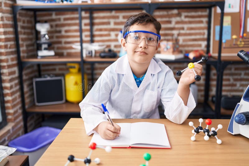 Adorable Hispanic Boy Student Writing on Notebook Holding Molecules at ...