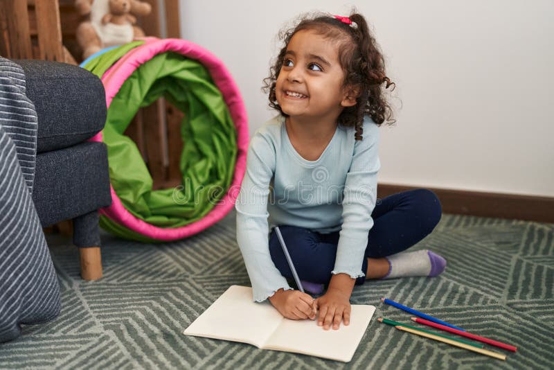 Adorable Hispanic Girl Drawing on Notebook Sitting on Floor at Home ...
