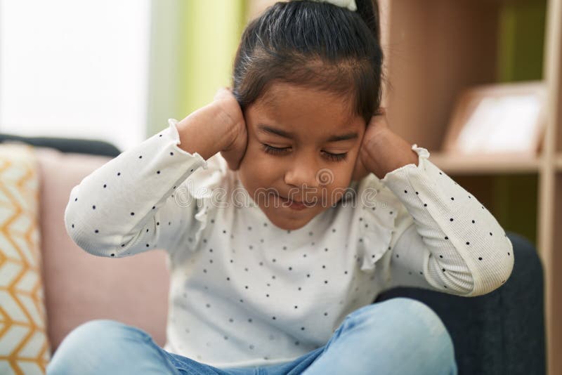 Adorable Hispanic Girl Sitting on Sofa with Hands on Ears at Home Stock ...