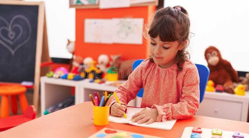 Adorable Hispanic Girl Student Sitting on Table Drawing on Notebook at ...