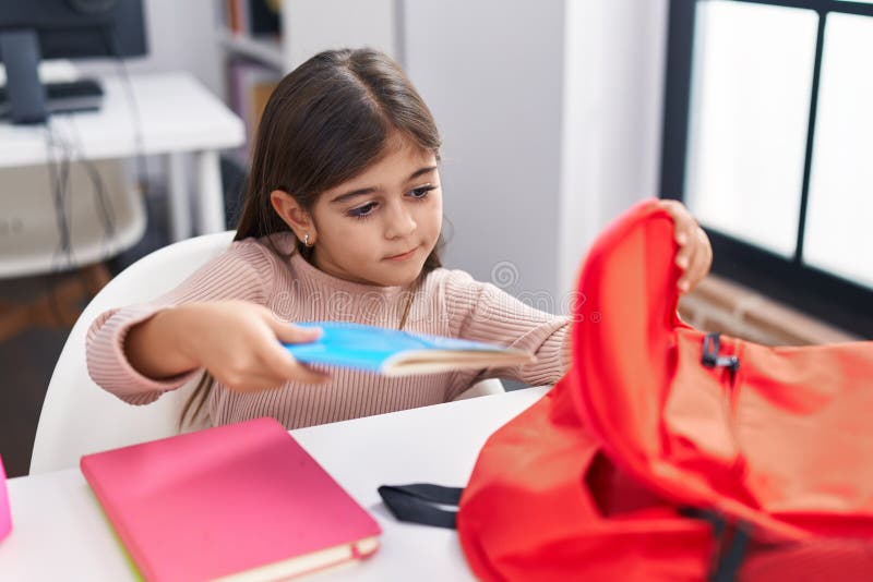 Adorable Hispanic Girl Student Sitting on Table Putting Book on ...