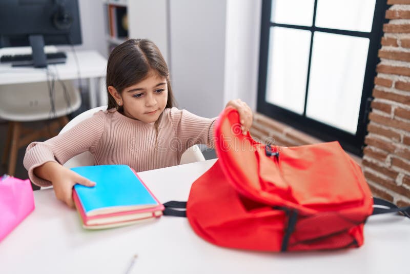 Adorable Hispanic Girl Student Sitting on Table Putting Book on ...