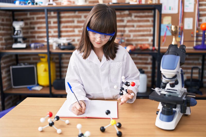 Adorable Hispanic Girl Student Writing on Notebook Holding Molecules at ...