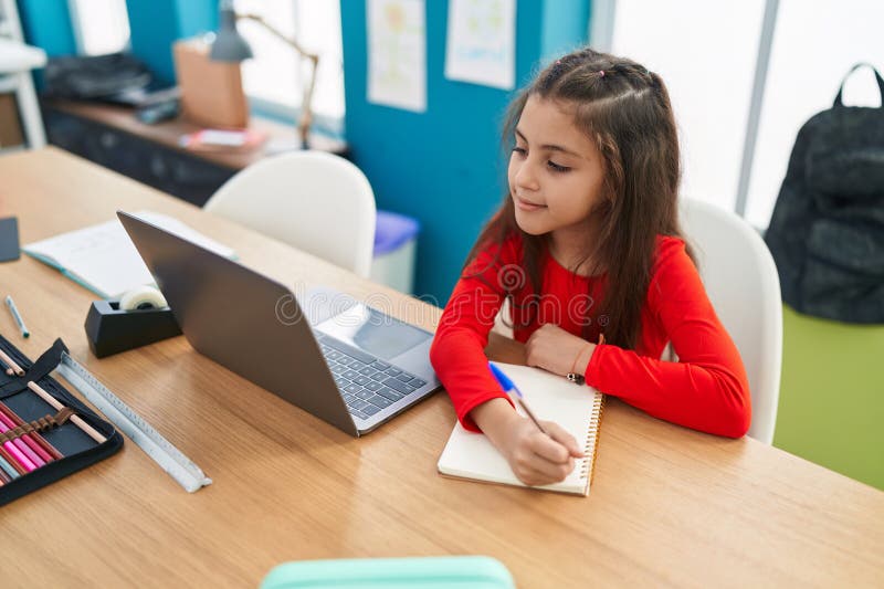 Adorable Hispanic Girl Student Writing on Notebook Using Laptop at ...