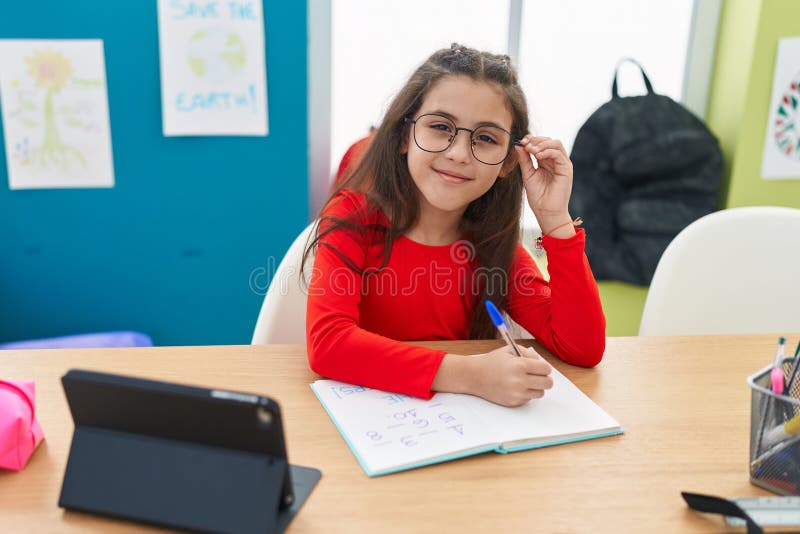 Adorable Hispanic Girl Student Writing on Notebook Using Touchpad at ...