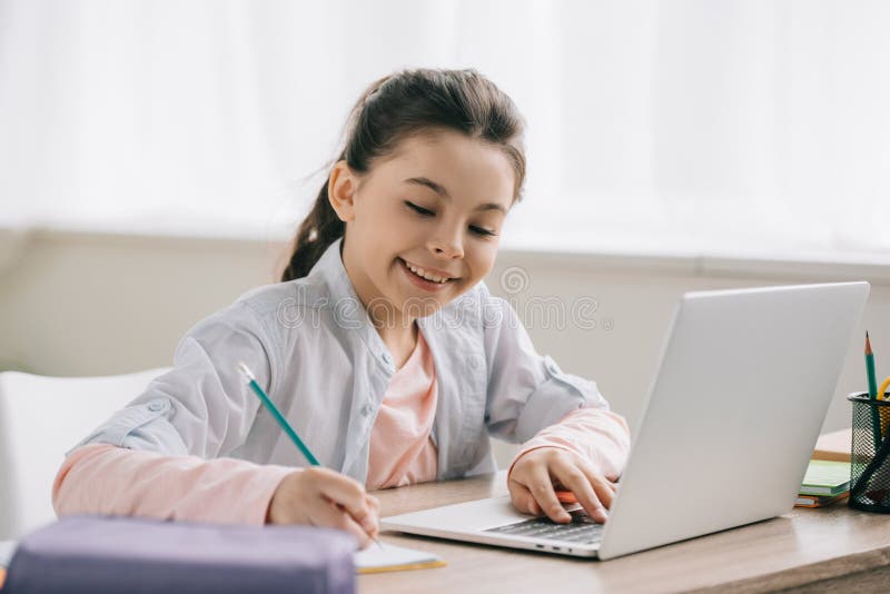 Smiling Child Writing in Copy Book and Using Laptop while Doing ...