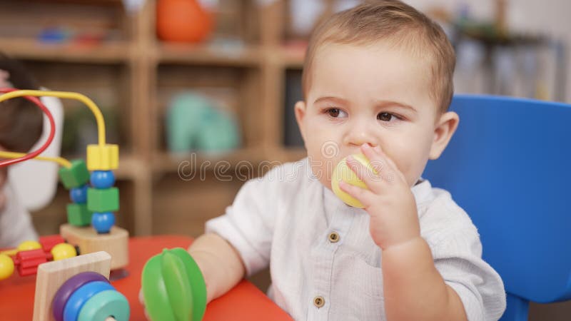 Adorable Toddler Bitting Plastic Toy Sitting on Table at Kindergarten ...