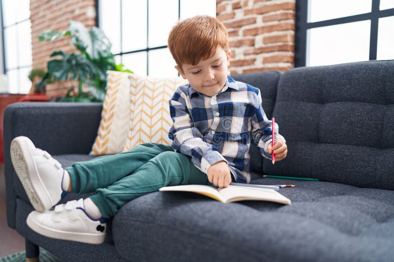 Adorable Toddler Drawing on Notebook Sitting on Sofa at Home Stock ...