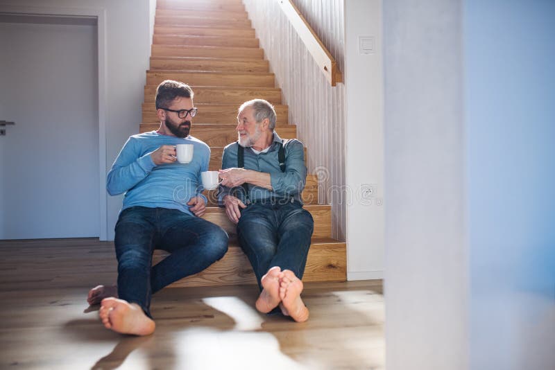 An Adult Hipster Son And Senior Father Sitting On Stairs Indoors At