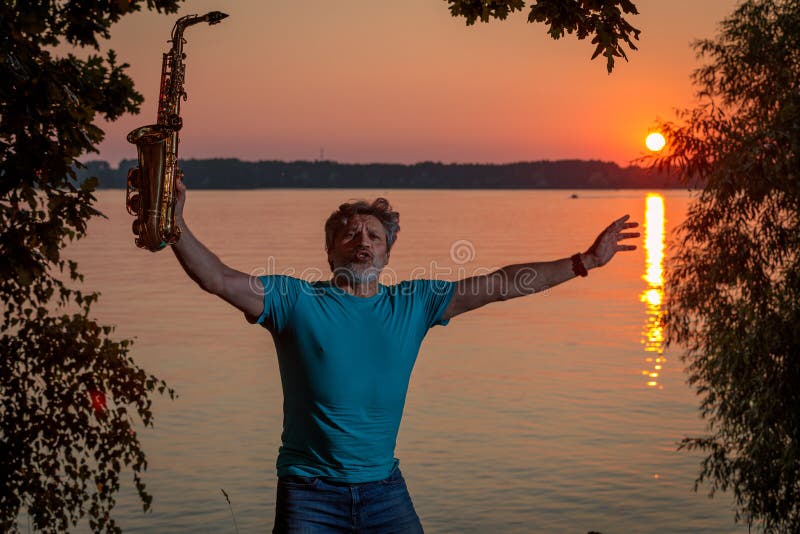 An Adult Man Plays the Saxophone at Sunset by the River in the Evening ...