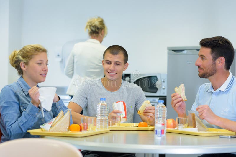 Adults Sat Around Table Eating Packed Lunches Off Trays Stock Photo ...