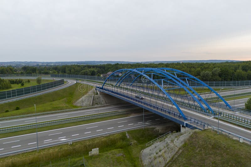 Aerial View of a Modern Blue Arch Bridge Over a Highway Surrounded by ...