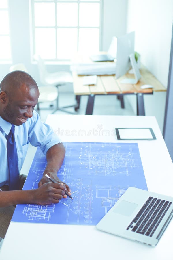 African American Architect Working with Computer and Blueprints in ...