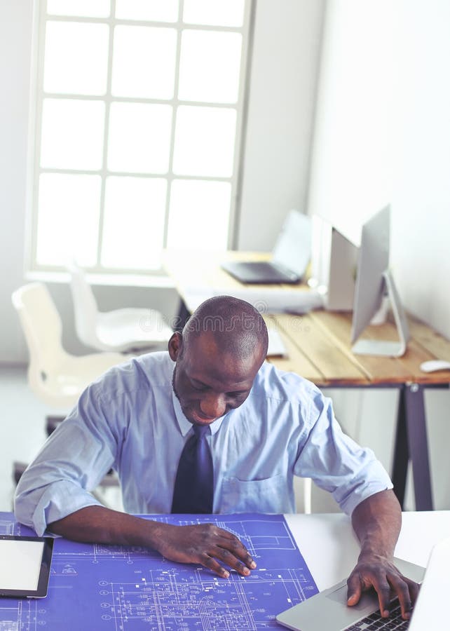 African American Architect Working with Computer and Blueprints in ...