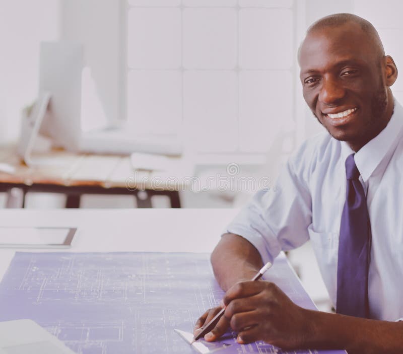 African American Architect Working with Computer and Blueprints in ...