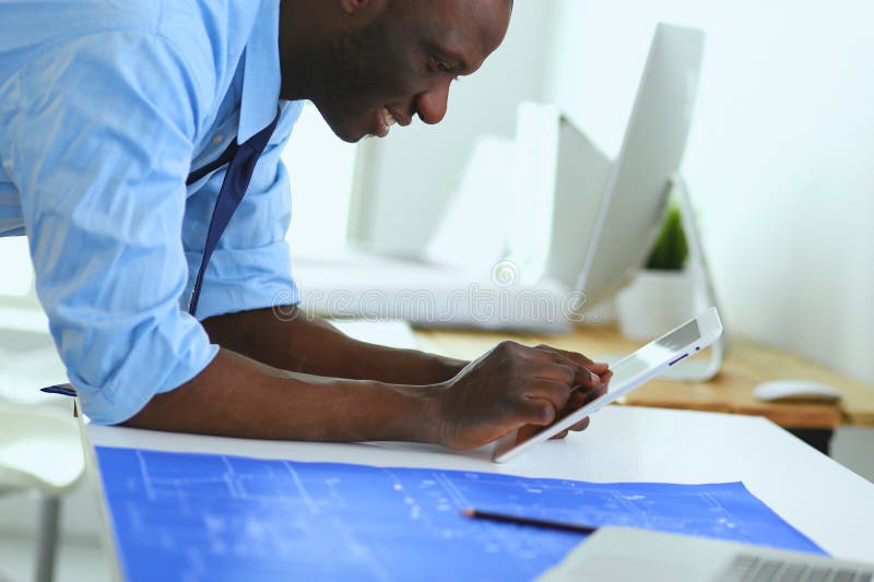 African American Architect Working with Computer and Blueprints in ...