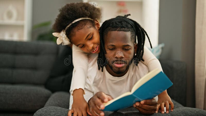 African American Father and Daughter Lying on Sofa Reading Book at Home ...