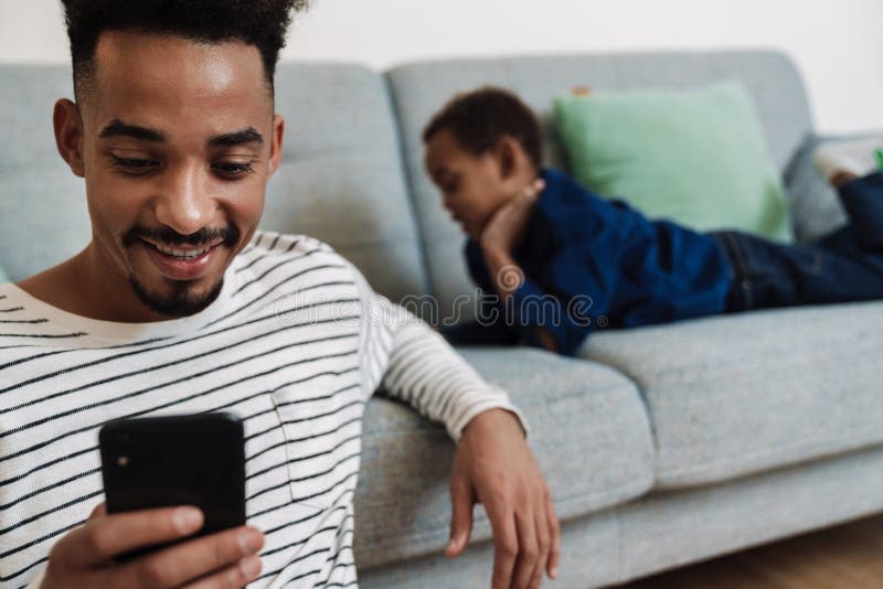 African American Father and Son Using Mobile Phone while Resting Stock ...