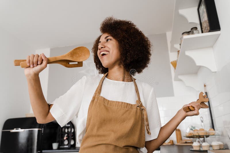 African American Housewife In Apron Singing With Spatulas For Cooking