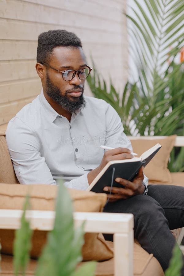 African American Man With Glasses Holds Notebook In Hands And Takes