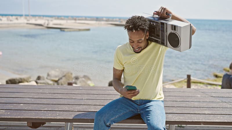 African American Man Holding Boombox Using Smartphone at Seaside Stock ...