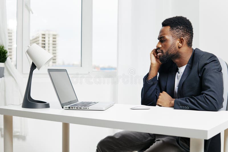 African American Man Multitasking at Desk with Laptop, Engaging in a ...