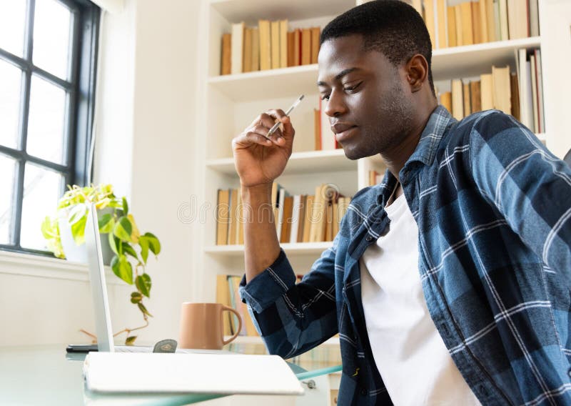 African American Man Studying at Home, Using Laptop and Taking Notes in ...