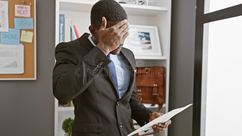 An African American Man in a Suit Stands Stressed in an Office Holding ...