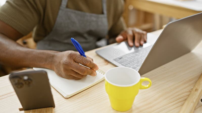 African American Man Taking Notes Next To Laptop in Workshop Stock ...
