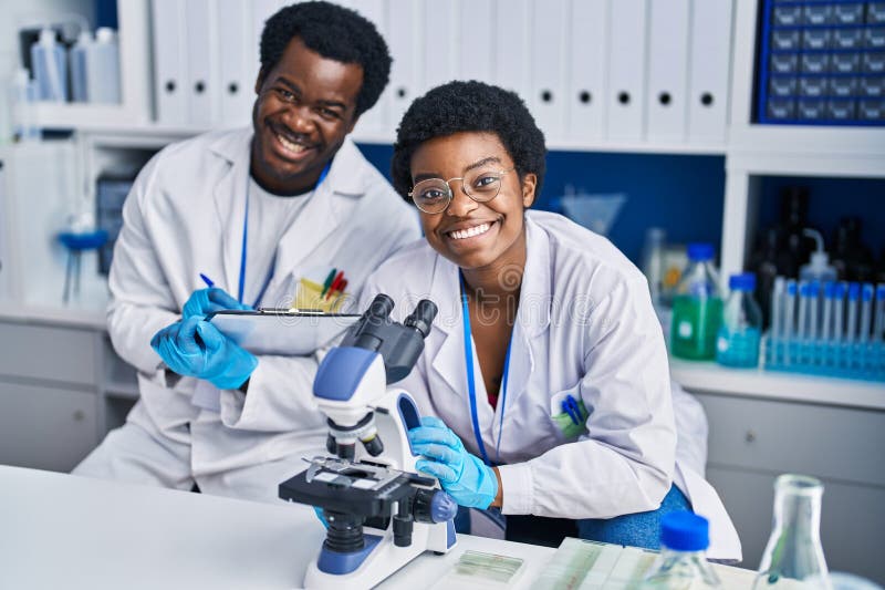 African American Man and Woman Scientists Using Microscope Writing on ...
