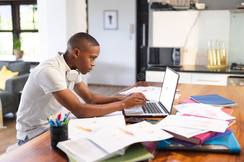 African American Teenage Boy Using Computer and Doing Lessons at Home ...